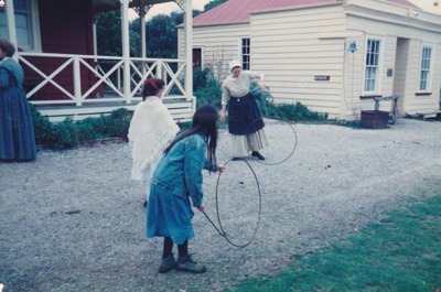 Two girls being shown how to roll a hoop with an iron hoop and skimmer ...