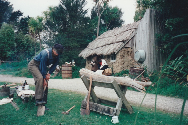 A man in costume digging in the grass in front of the Sod Cottage ...