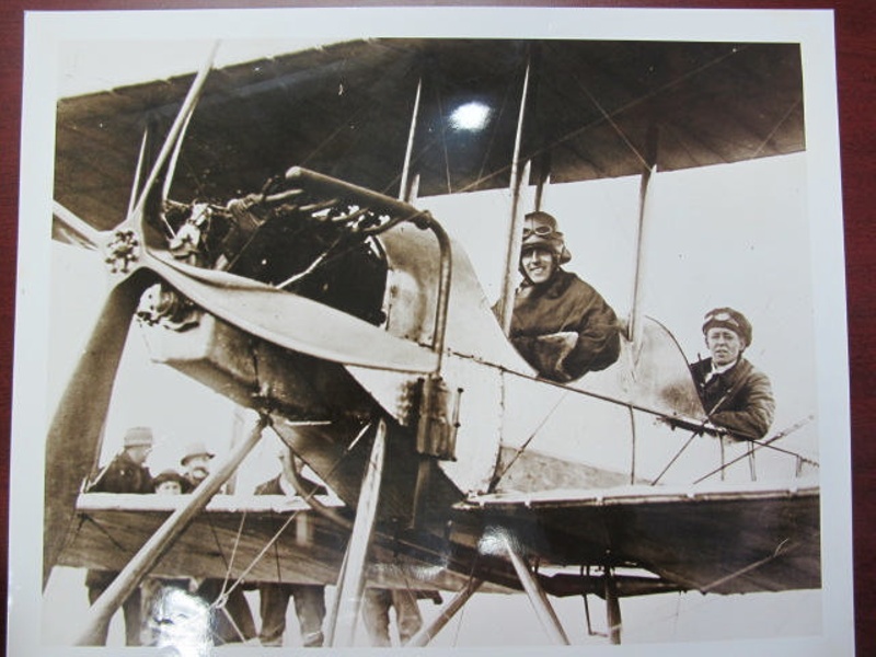 Photograph two military men in the cockpit of a bi-plane with onlookers ...
