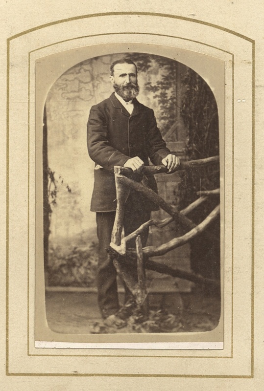 Studio photo of a formally attired bearded gentleman standing beside a ...