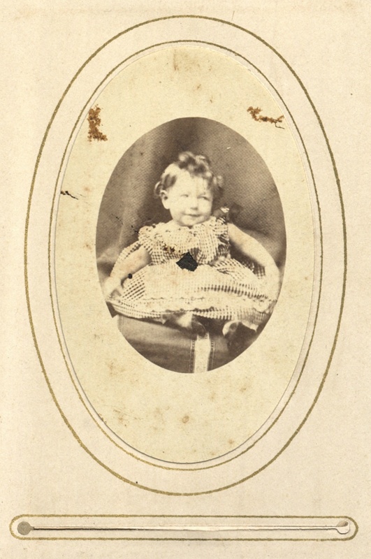 Studio photo of a baby girl dressed in a checked dress.; J.Hubert ...