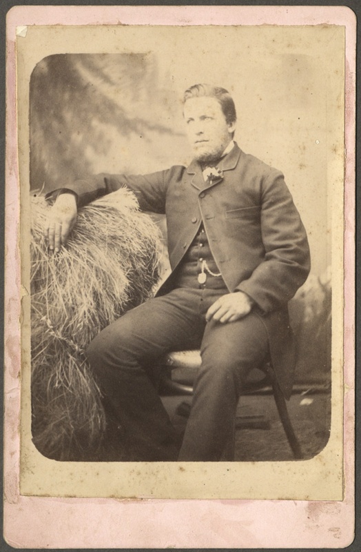 Studio photo of a young gentleman in formal attire seated next to a hay ...