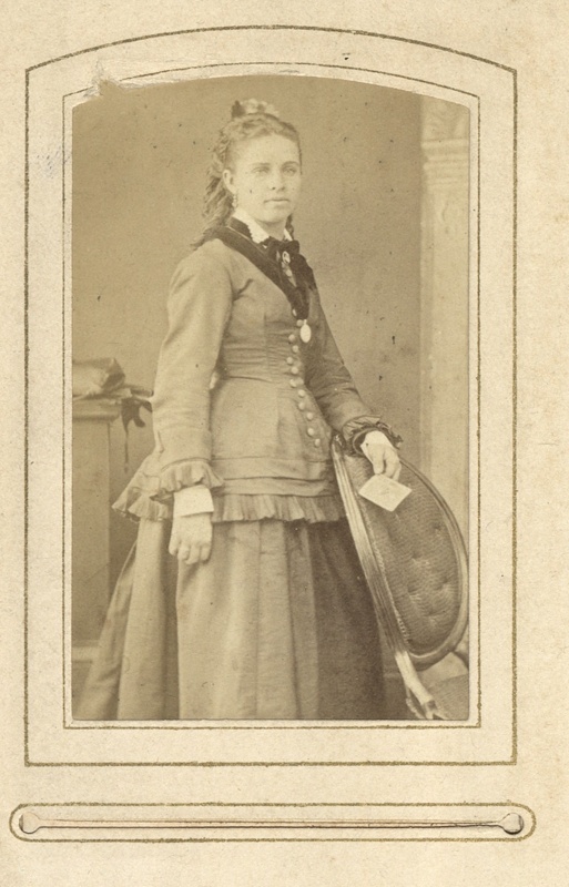 Studio photo of a formally dressed lady posing beside a chair.; J ...