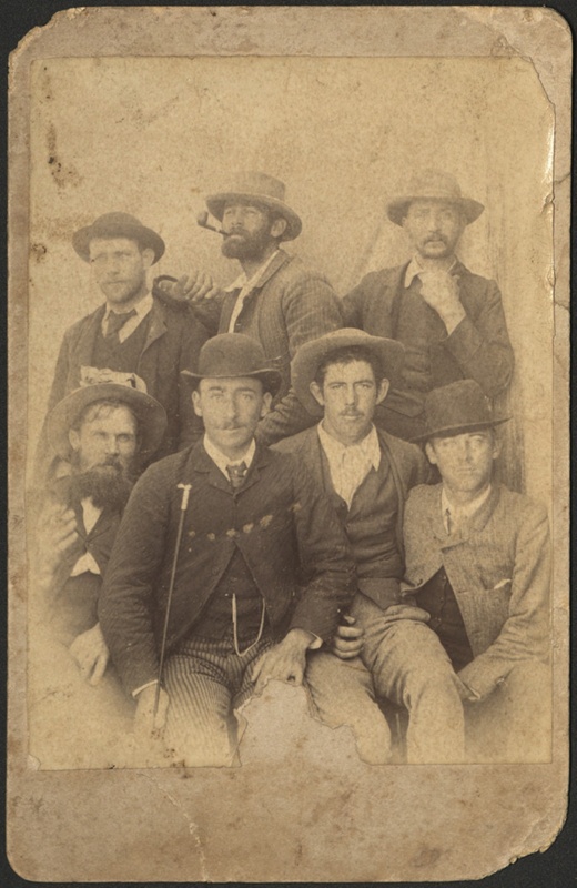 A group studio photo of seven casually dressed hatted men in seated and ...