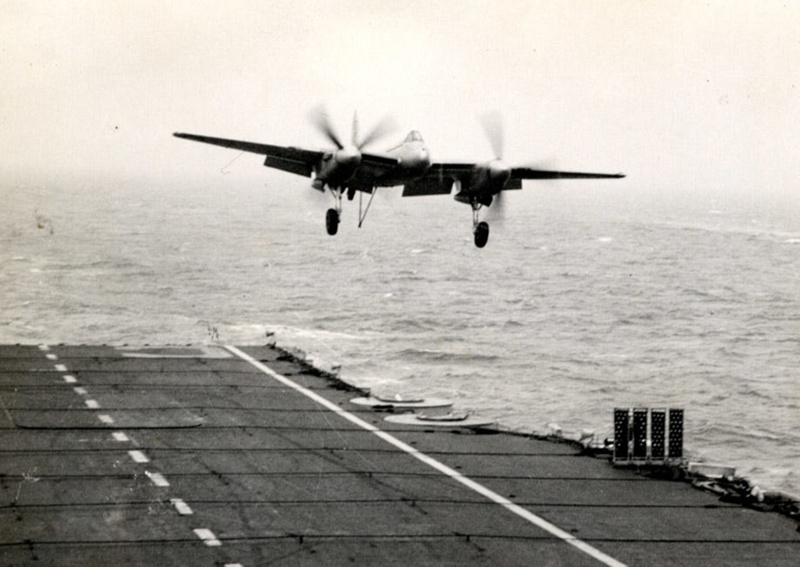 Photograph of a twin prop plane flying over the flightdeck of an ...